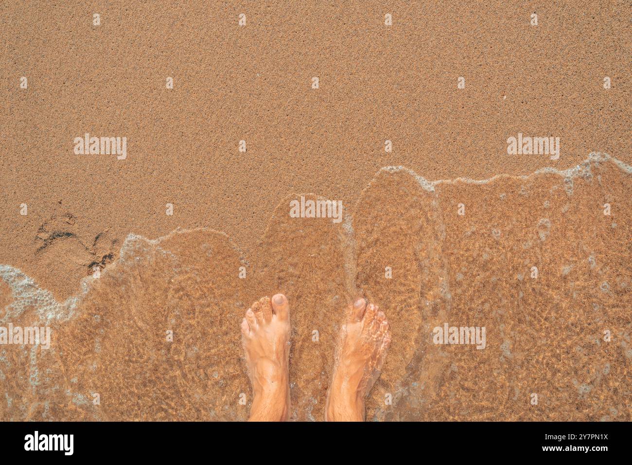 Barefoot male standing in wet sand on ocean beach on summer holiday ...