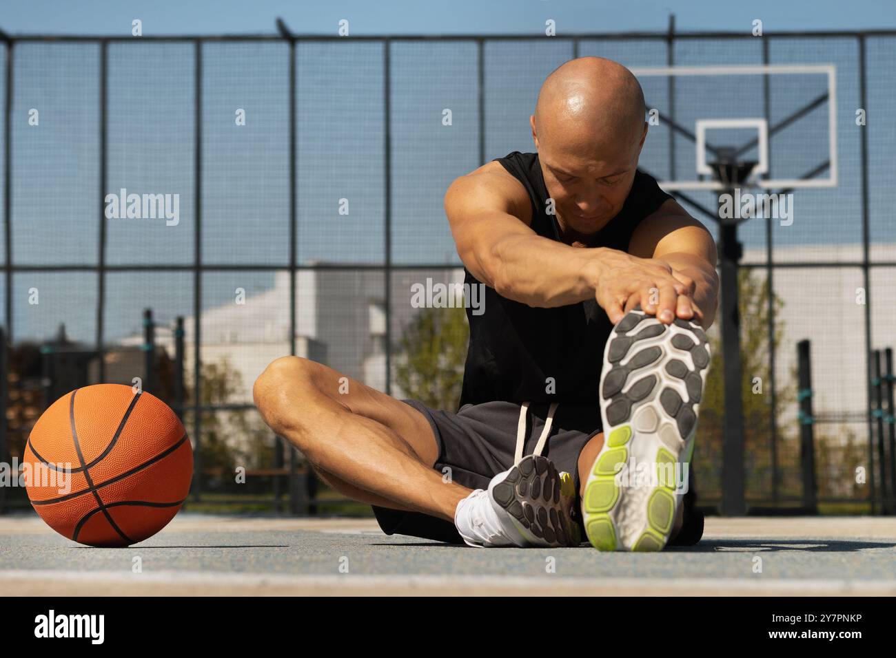 Basketball player stretching legs after game. Outdoors summer training ...
