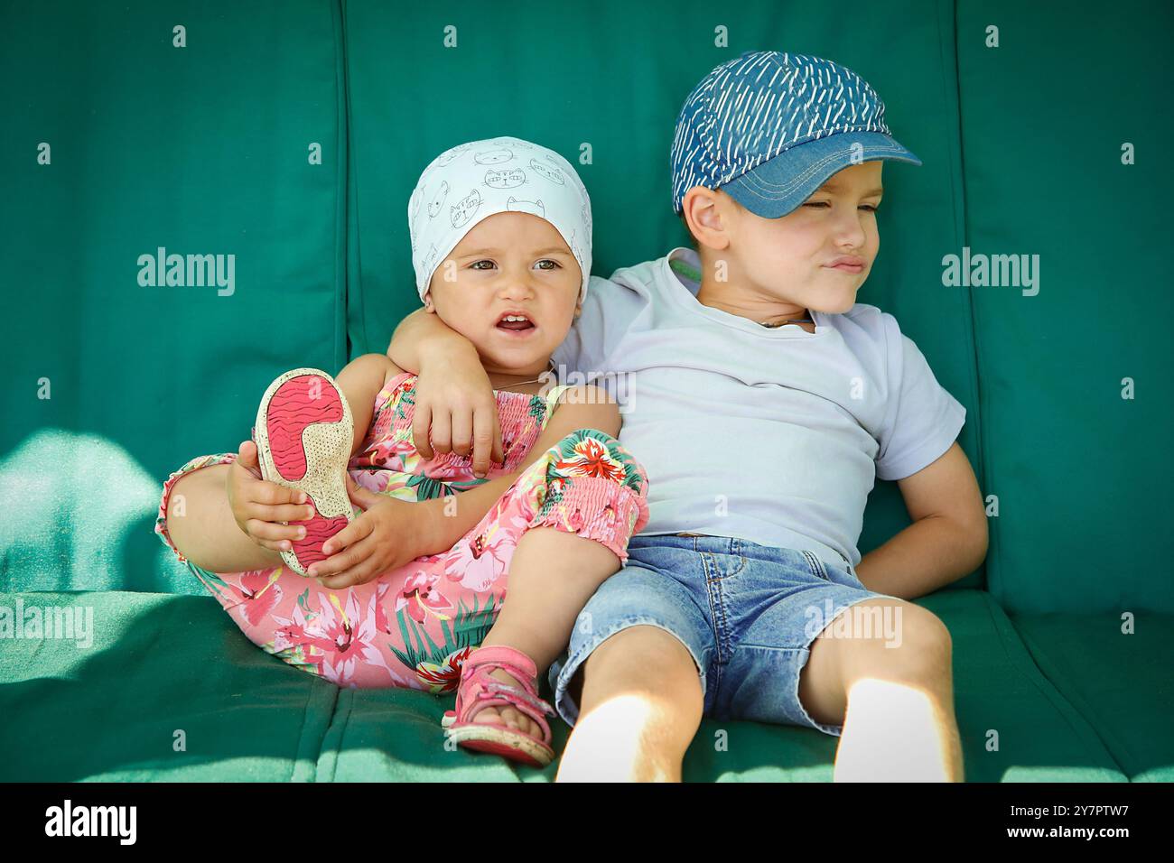 Boy and girl sitting and hugging on the green garden swing in the ...