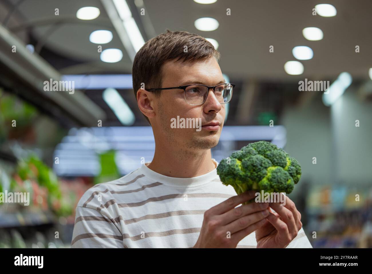 Man carefully examines fresh broccoli in the produce section of a ...