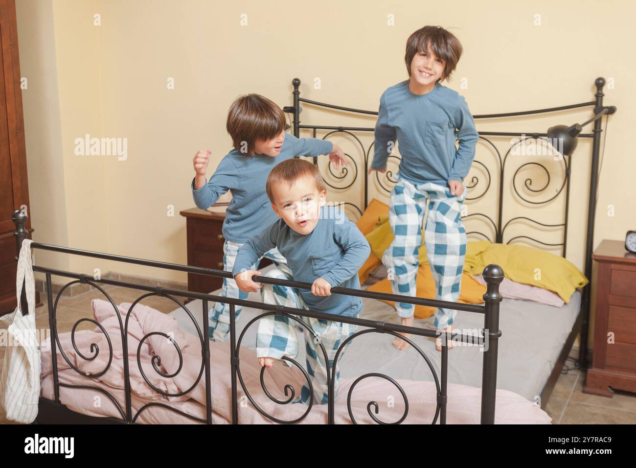 Three children are playing jumping jacks on the double bed in their ...