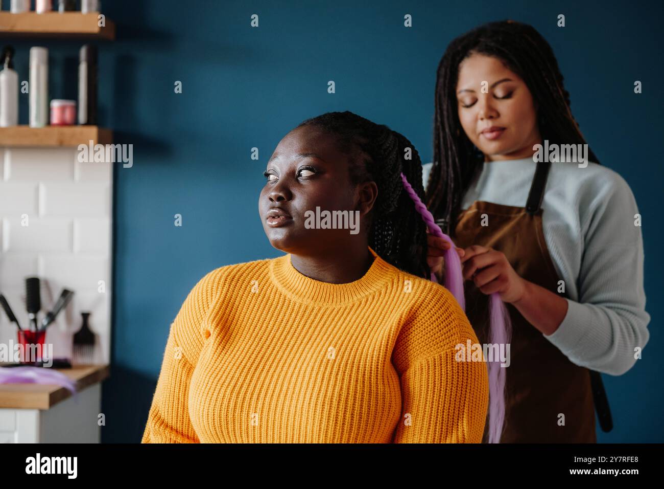 Confident African hairdresser braiding hair to female customer in salon ...