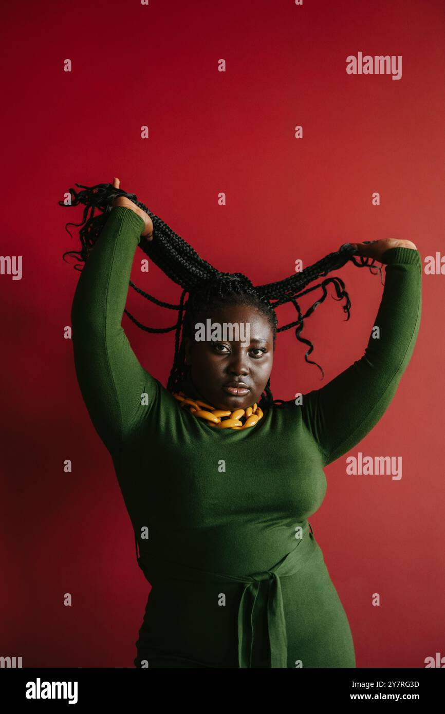 Beautiful plus size African woman adjusting her braided hair on red ...