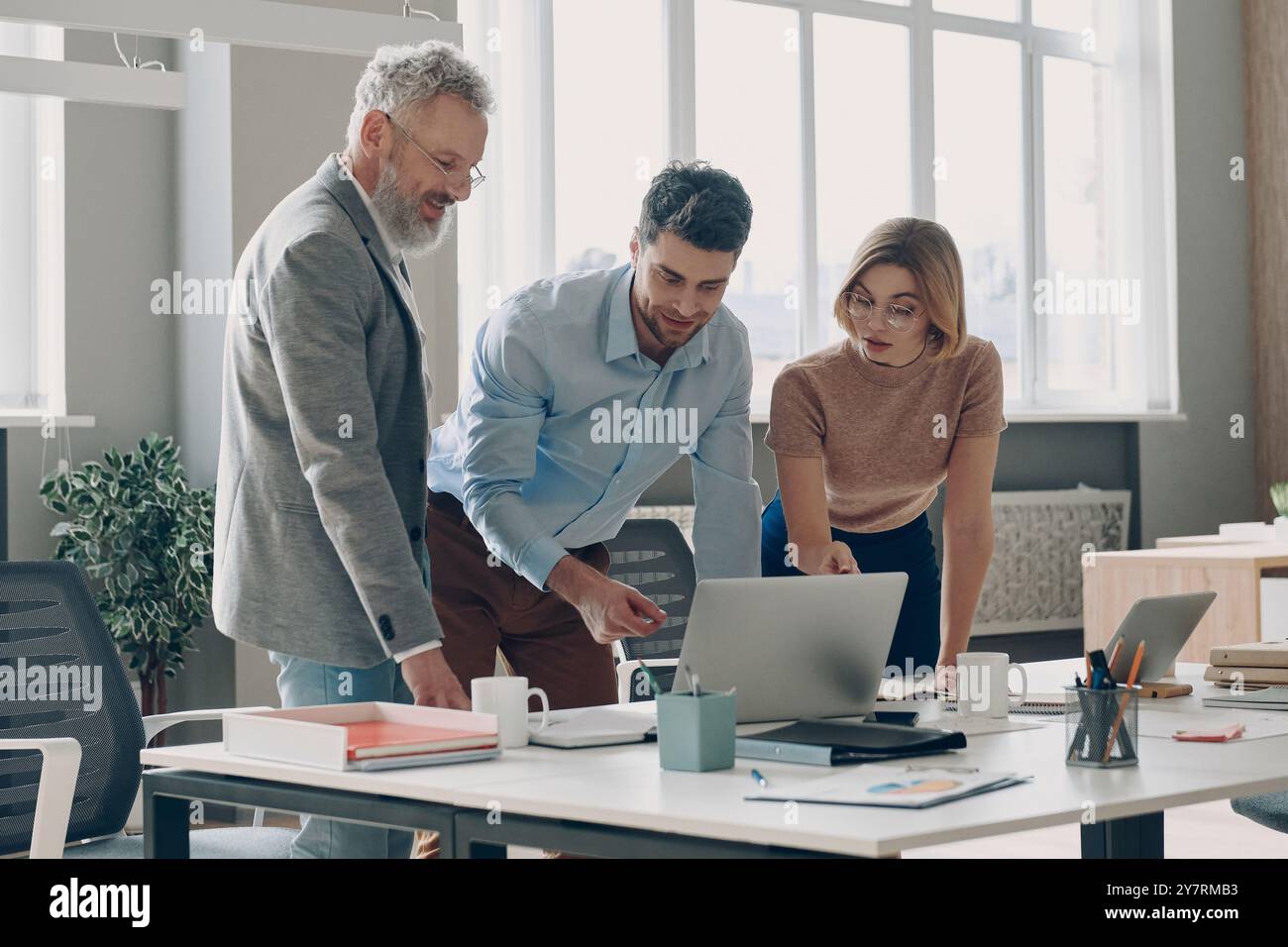Three confident business people having discussion while standing near ...