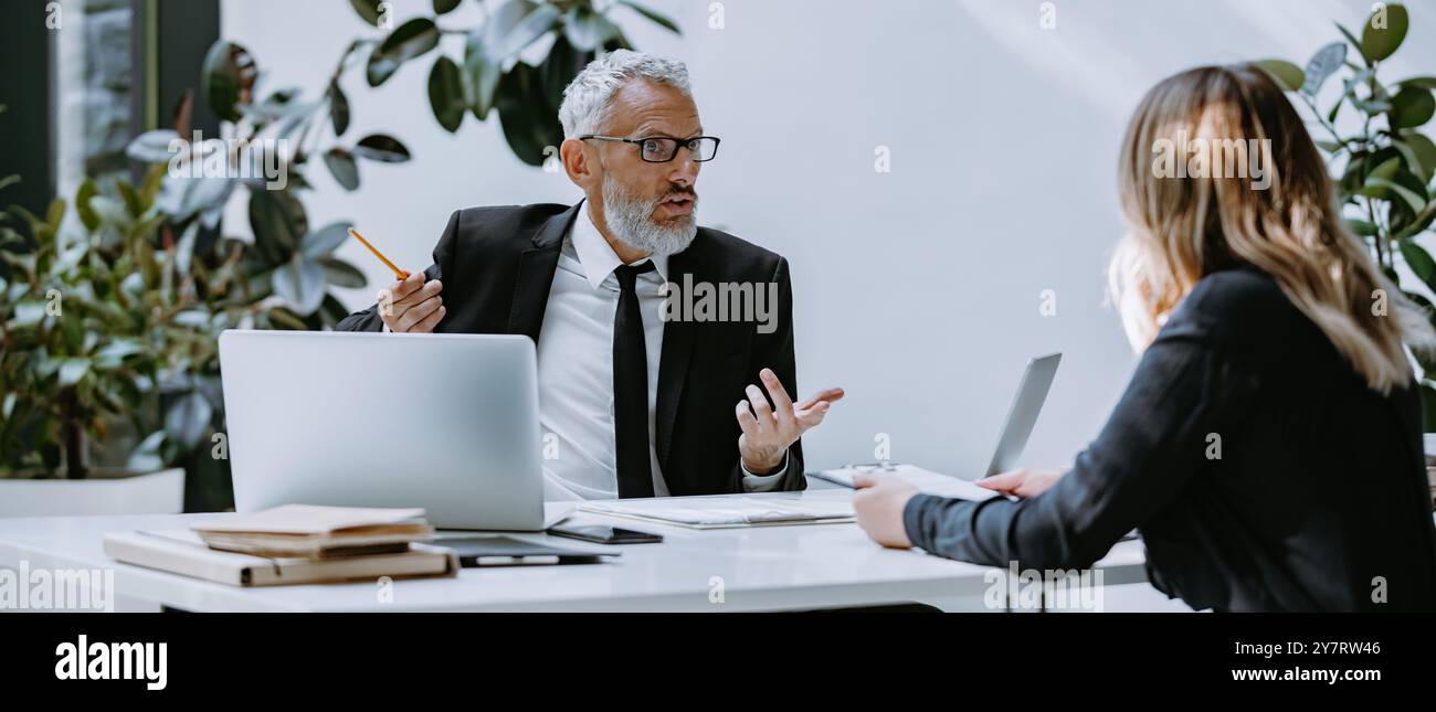 Confident mature man in formalwear interviewing job candidate while ...