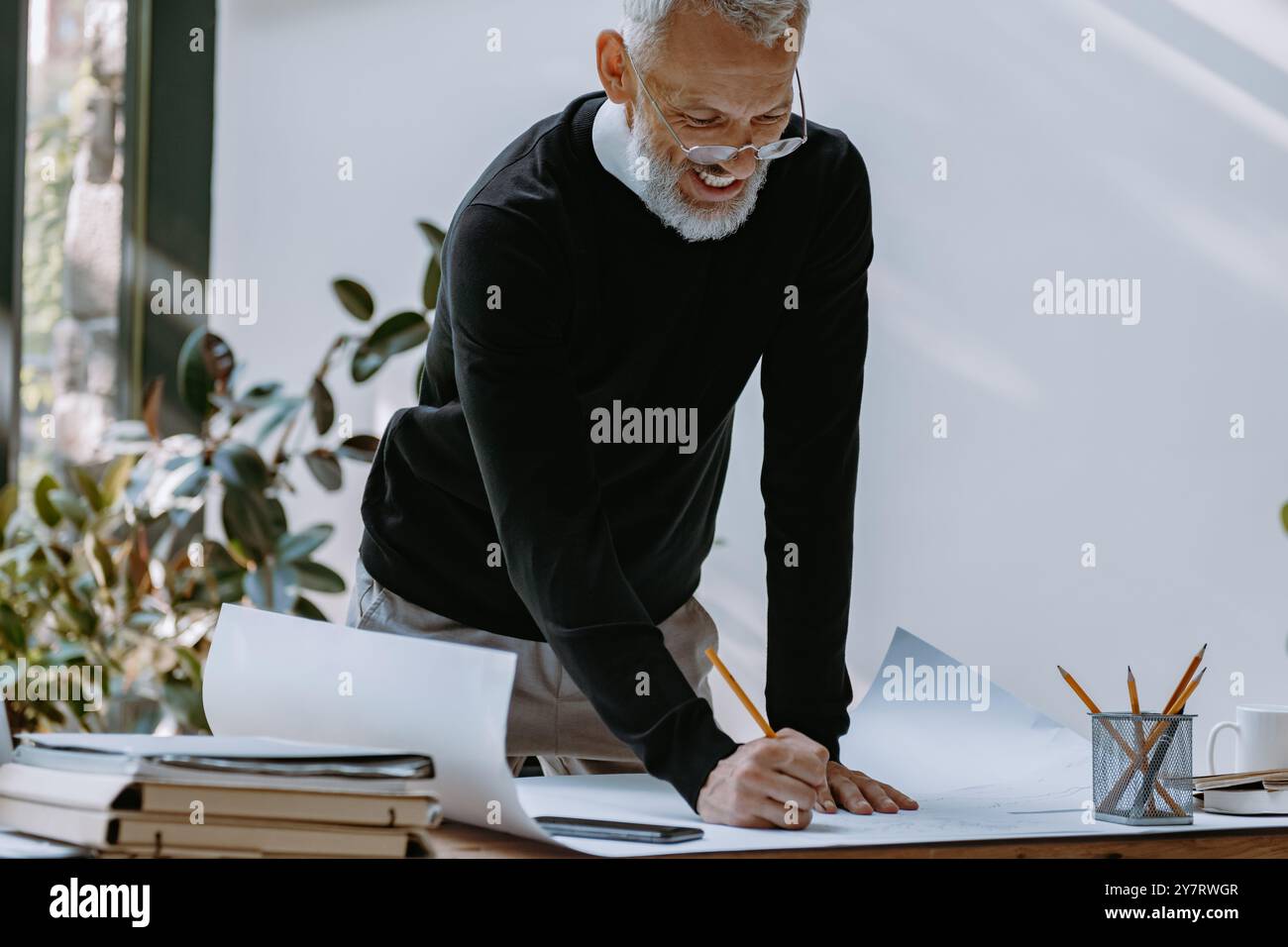 Confident mature architect drawing something on blueprint while working ...