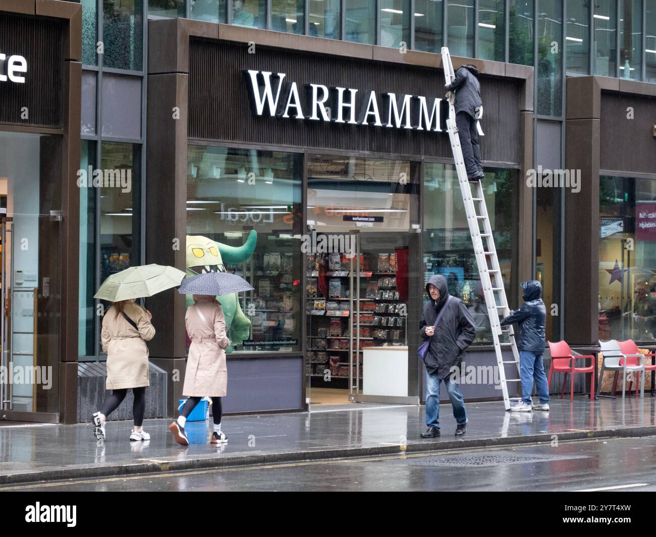 Cleaners on ladder cleaning sign in rain on Warhammer shop London UK ...