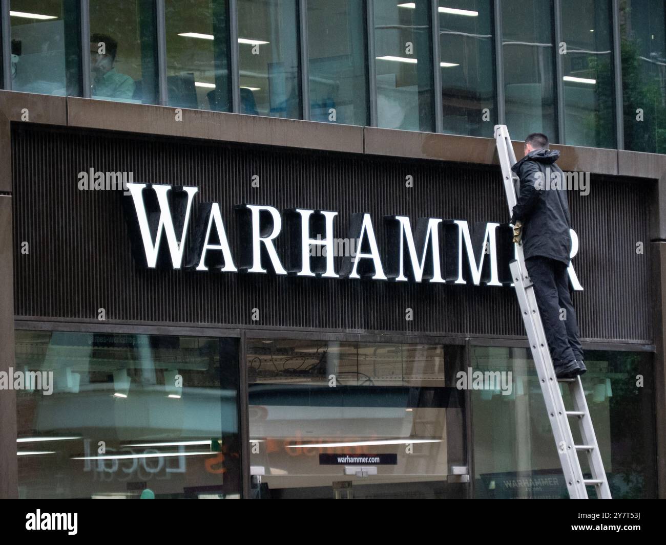 Cleaner on ladder cleaning sign in rain on Warhammer shop London UK ...