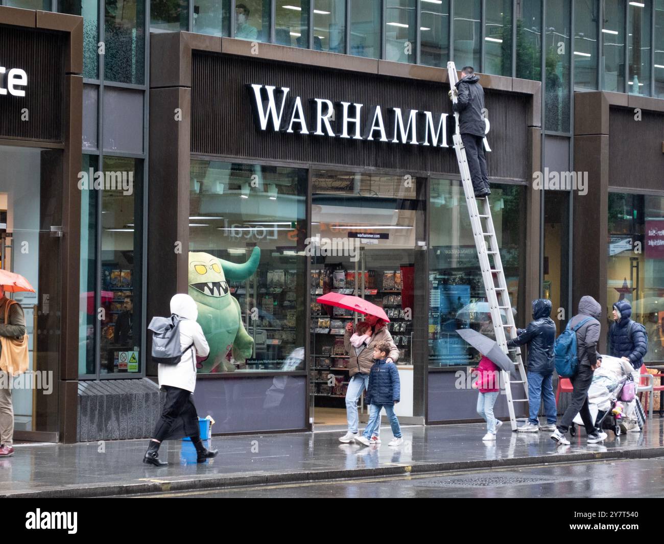 Cleaners on ladder cleaning sign in rain on Warhammer shop London UK ...