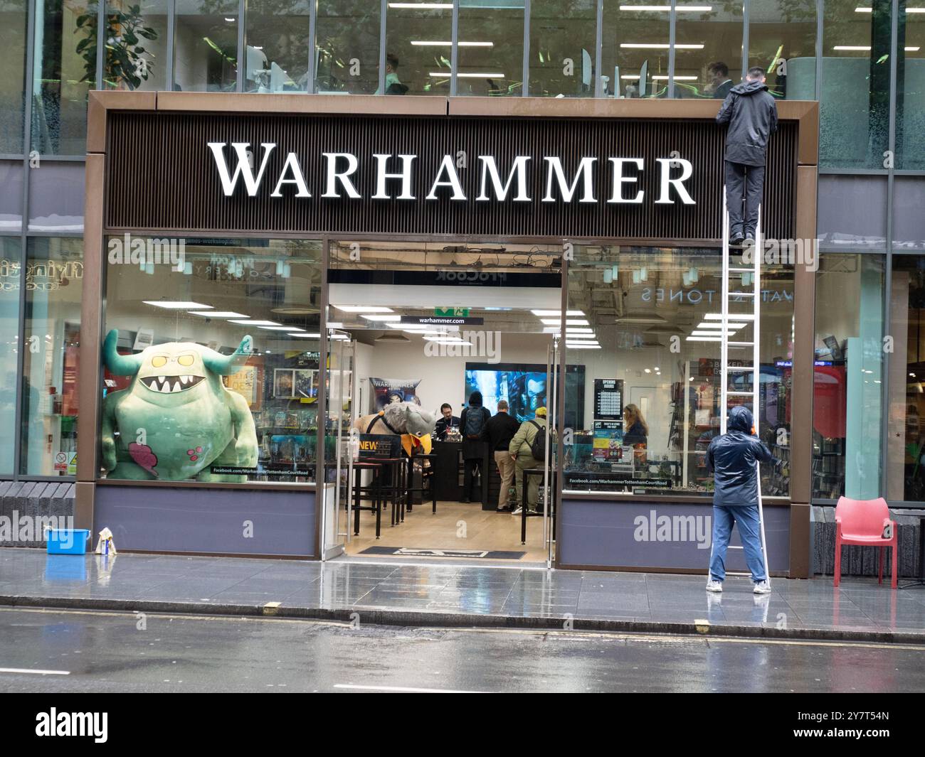 Cleaners on ladder cleaning sign in rain on Warhammer shop London UK ...