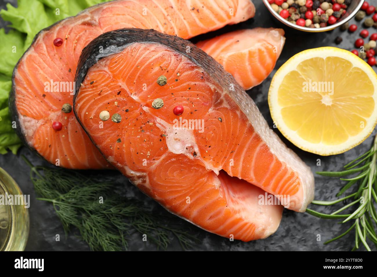 Fresh raw salmon steaks with spices and products on dark textured table ...