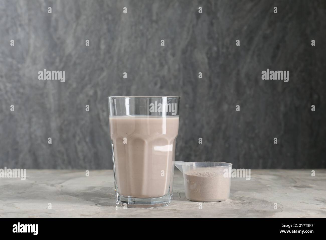Delicious protein shake in glass and scoop with powder on grey table ...