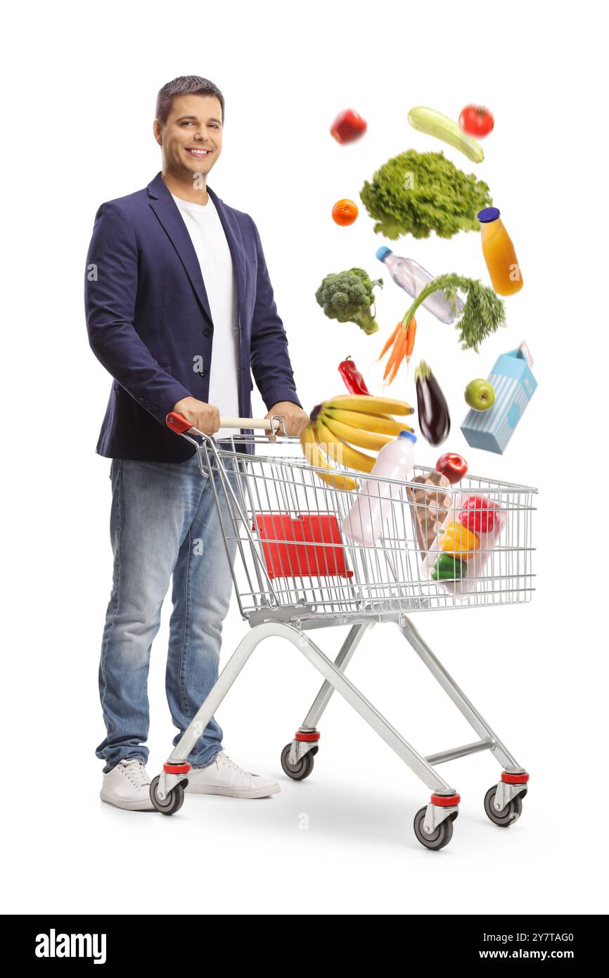Smiling man standing with a shopping cart and groceries falling in the ...