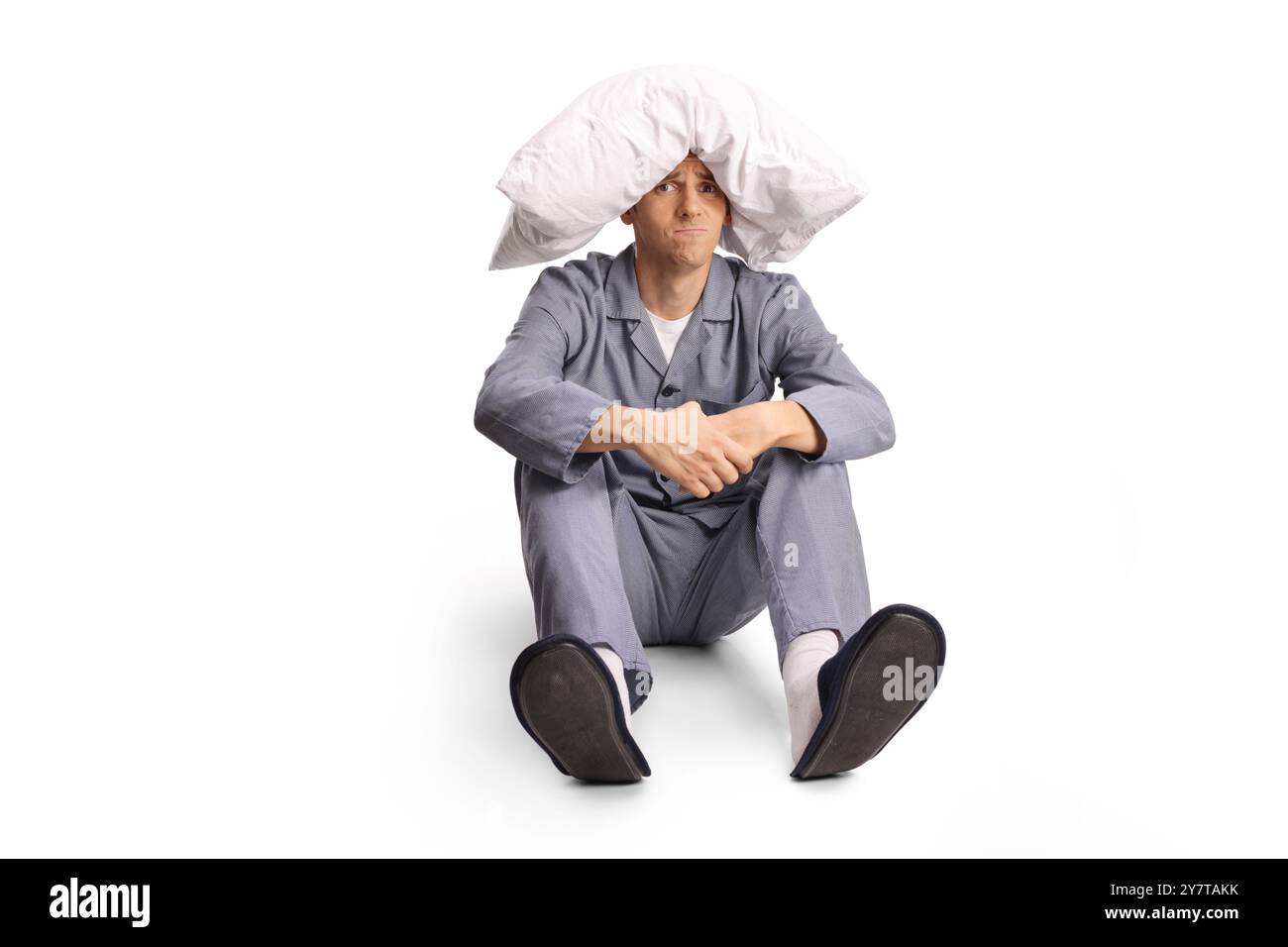 Angry young man in pajamas sitting on the ground with pillow over head ...
