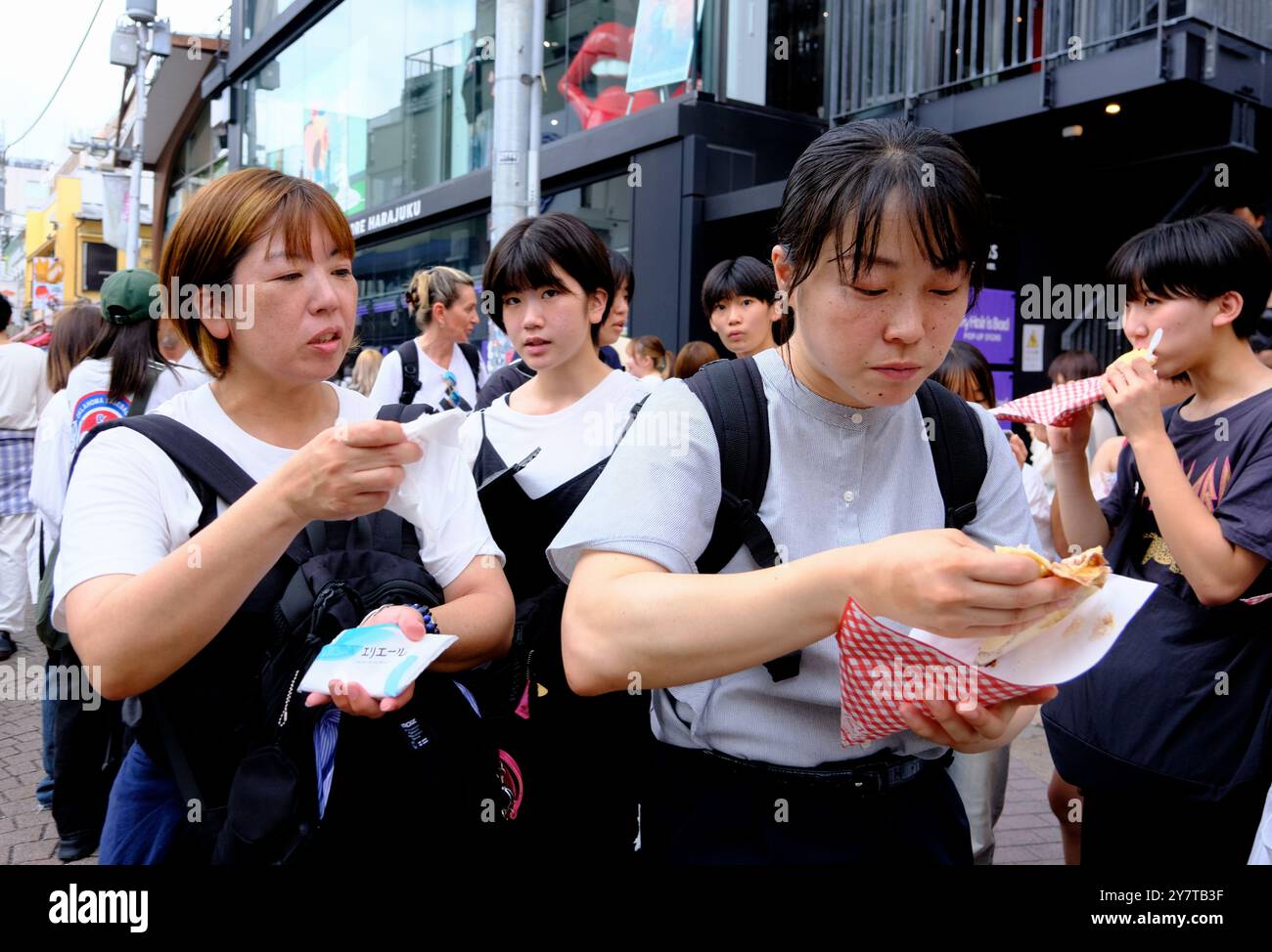 A group of female Japanese students eating pizza while they are walking ...