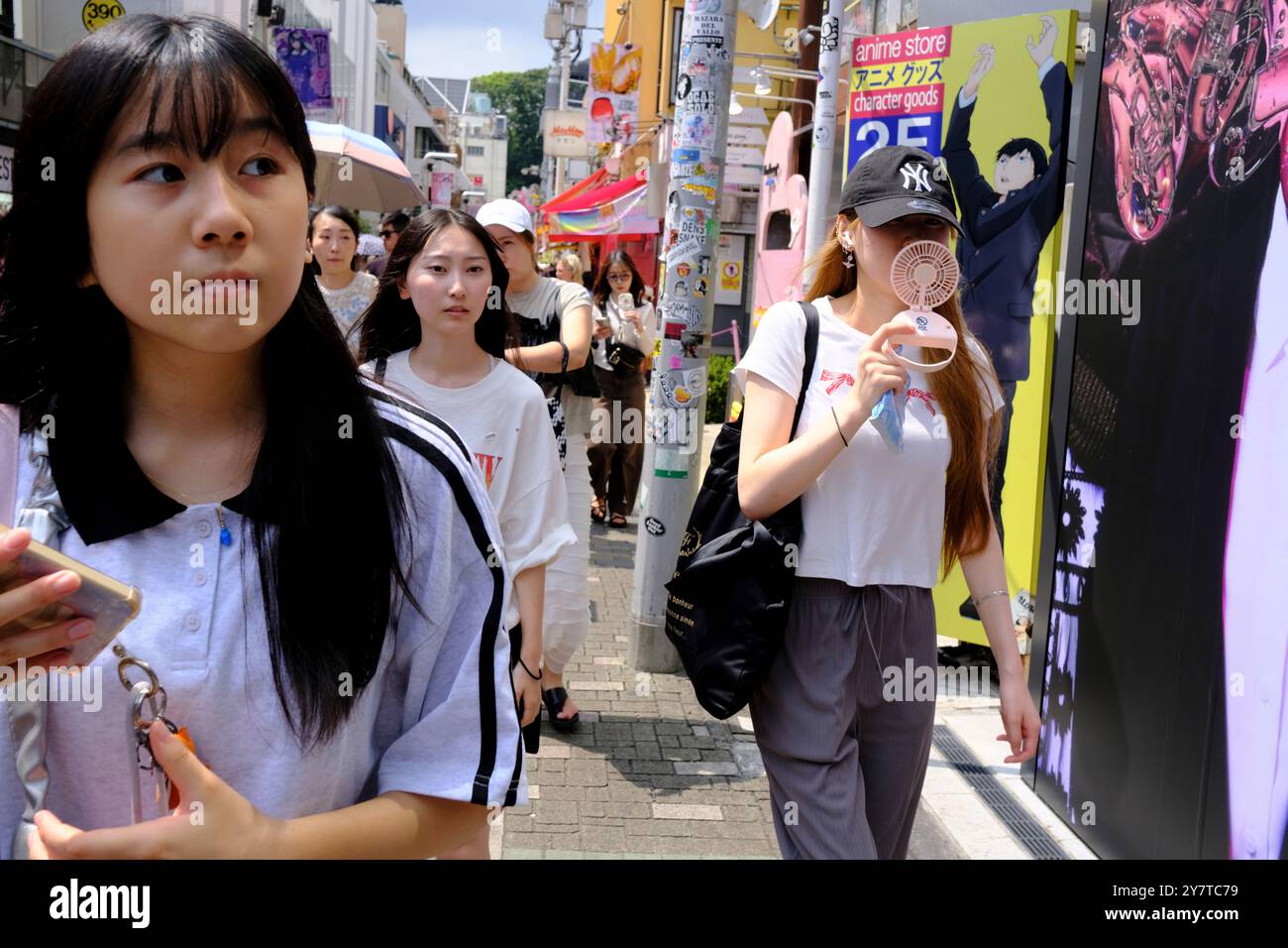A young woman using a hand held electric portable fan to cool herself ...