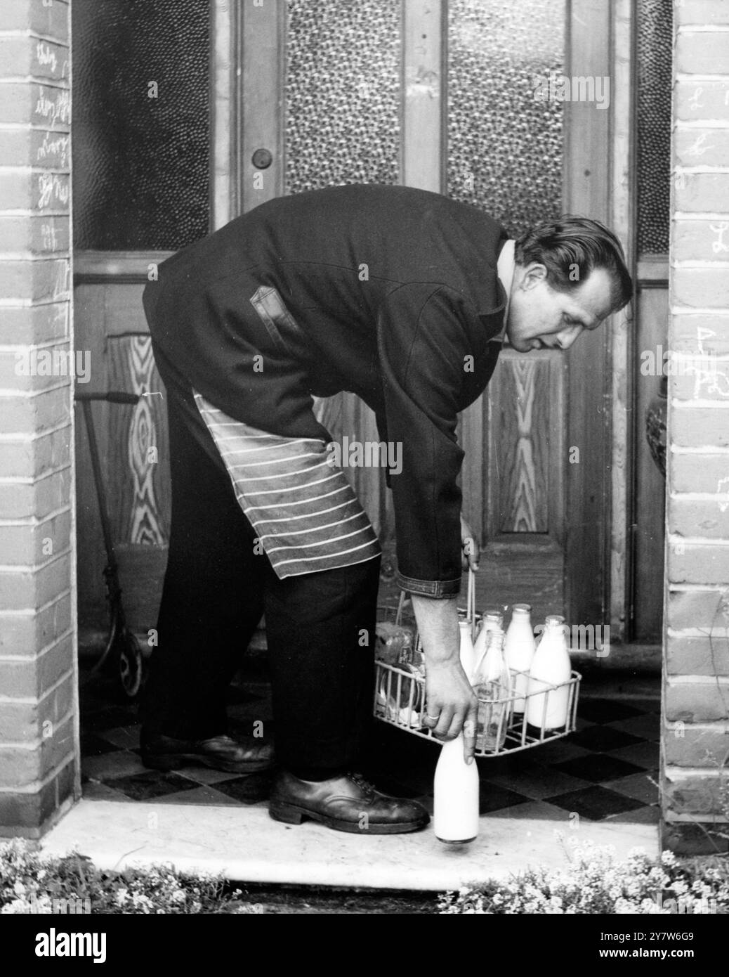 Milkman delivering milk bottles to the front door of a suburban house.3 ...