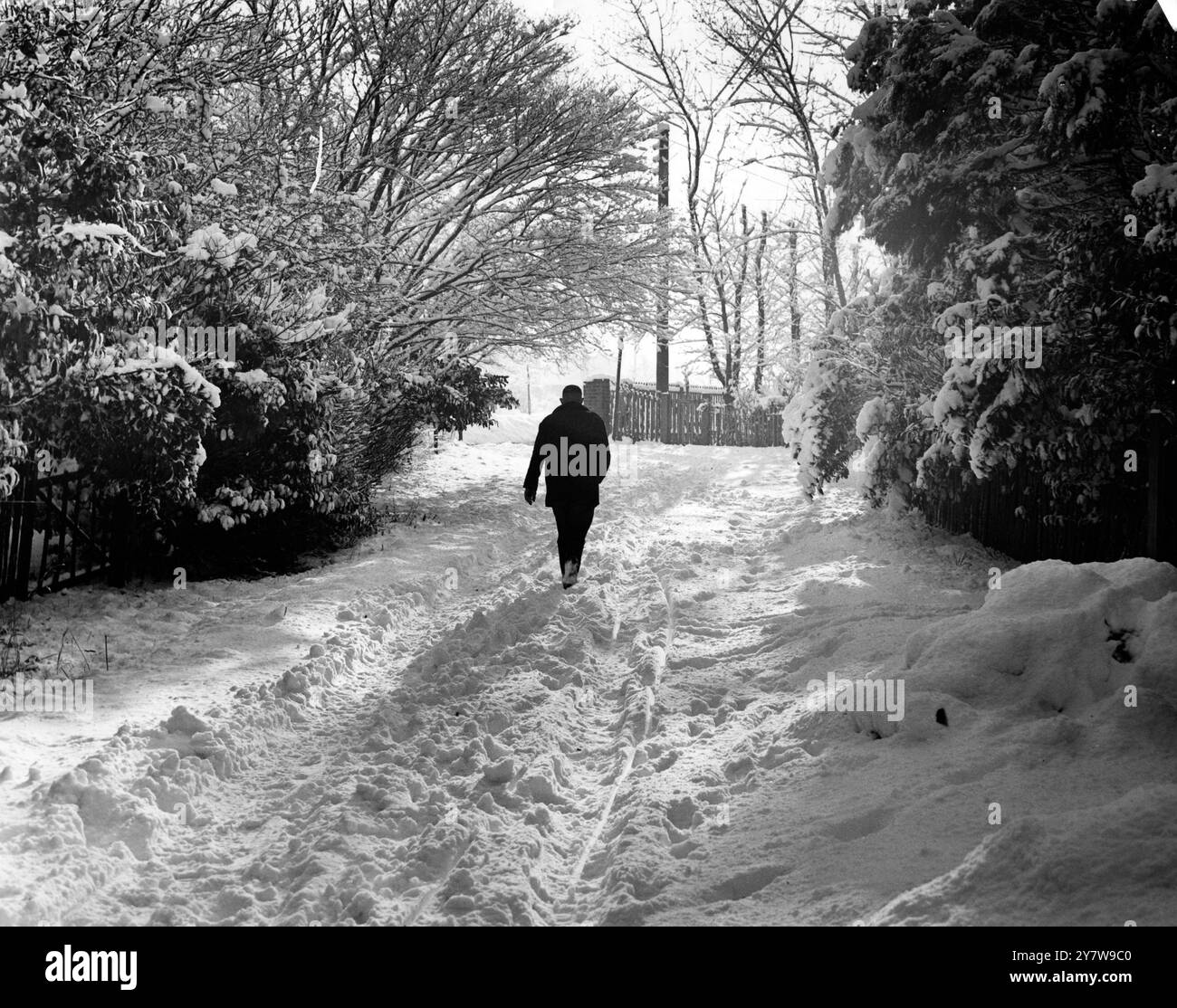 A man walking through deep snow on a path to a Kent village , England ...