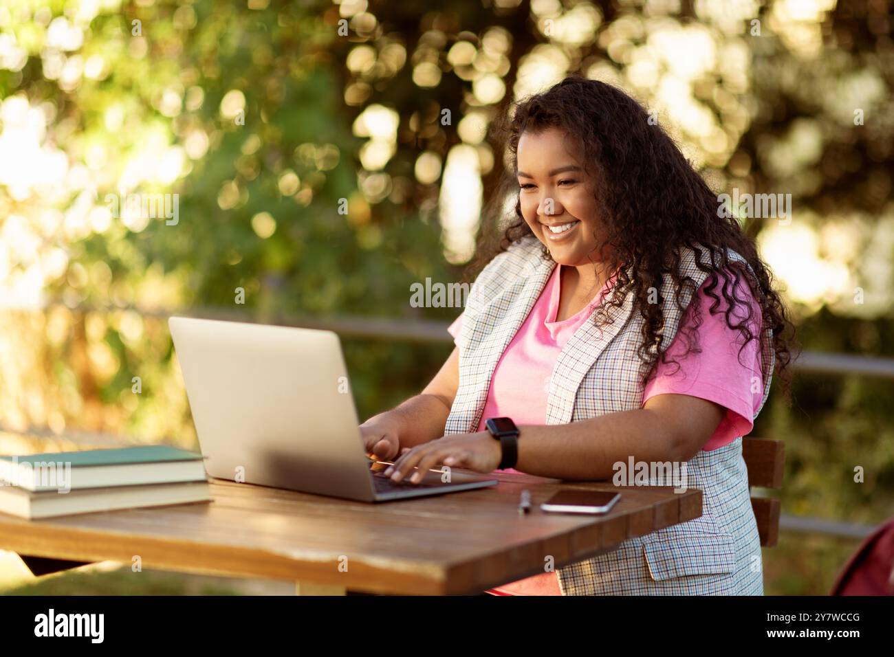 A woman enjoys working on her laptop at an outdoor table in the ...