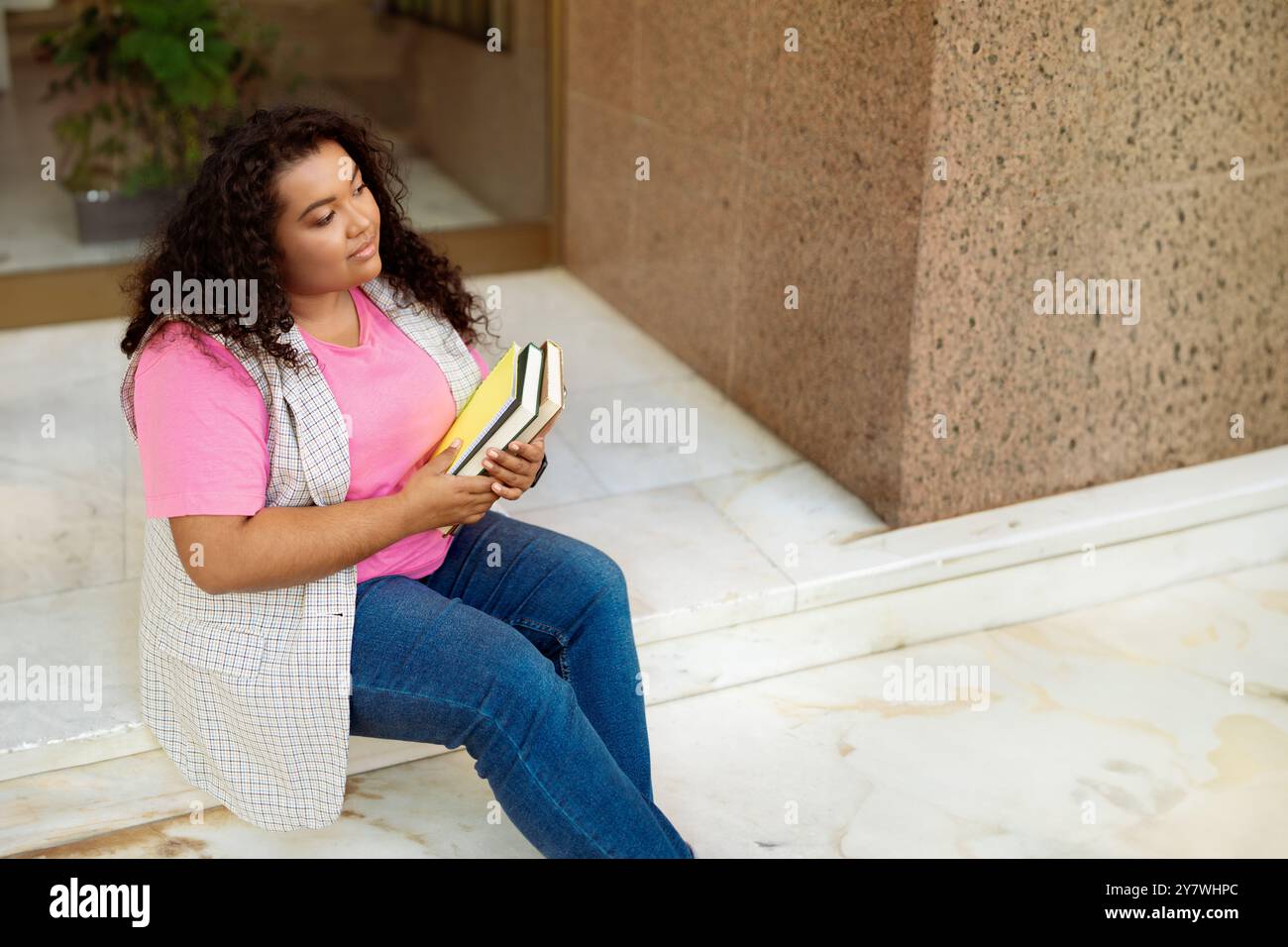 Young woman sitting on steps with books in her hands, enjoying a quiet ...