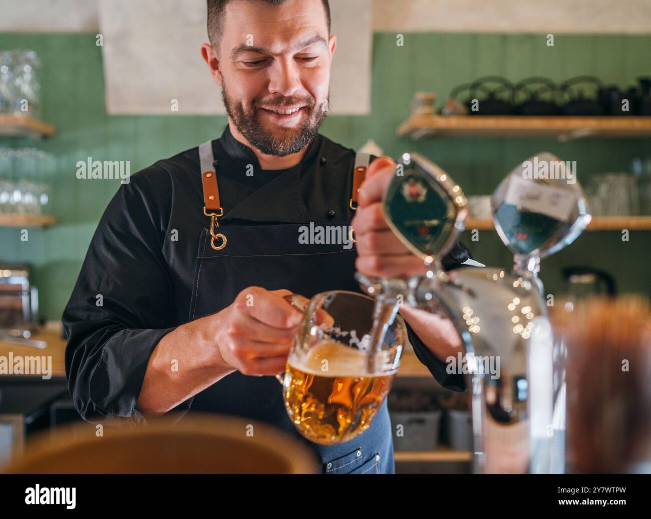 Smiling stylish bearded barman dressed black uniform with an apron ...