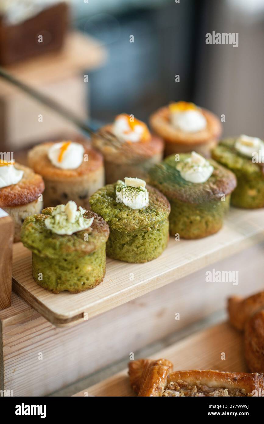 Decorated muffins are arranged on the counter of a coffee shop. Side ...