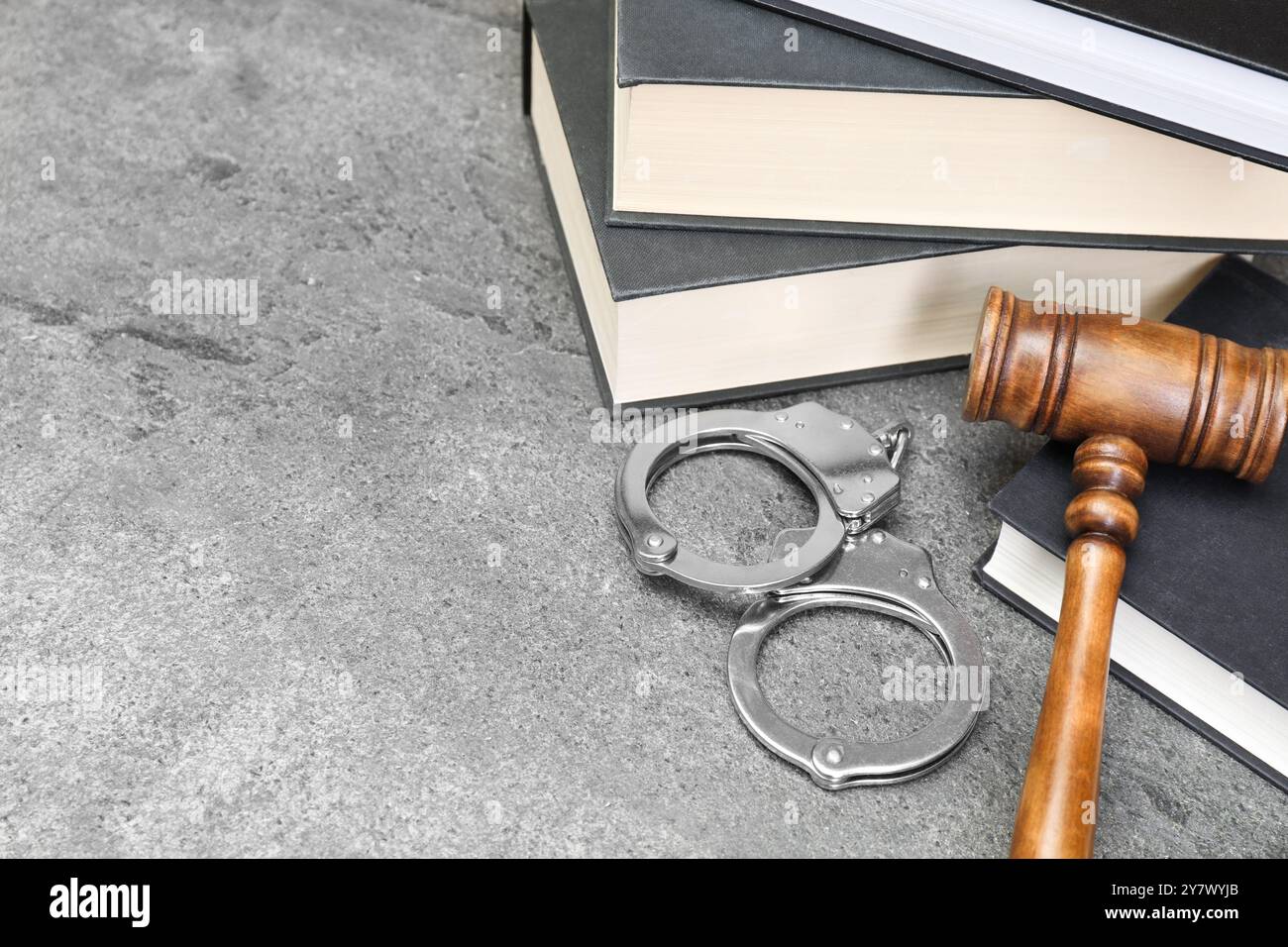 Books, judge's gavel and handcuffs on gray textured table, space for ...