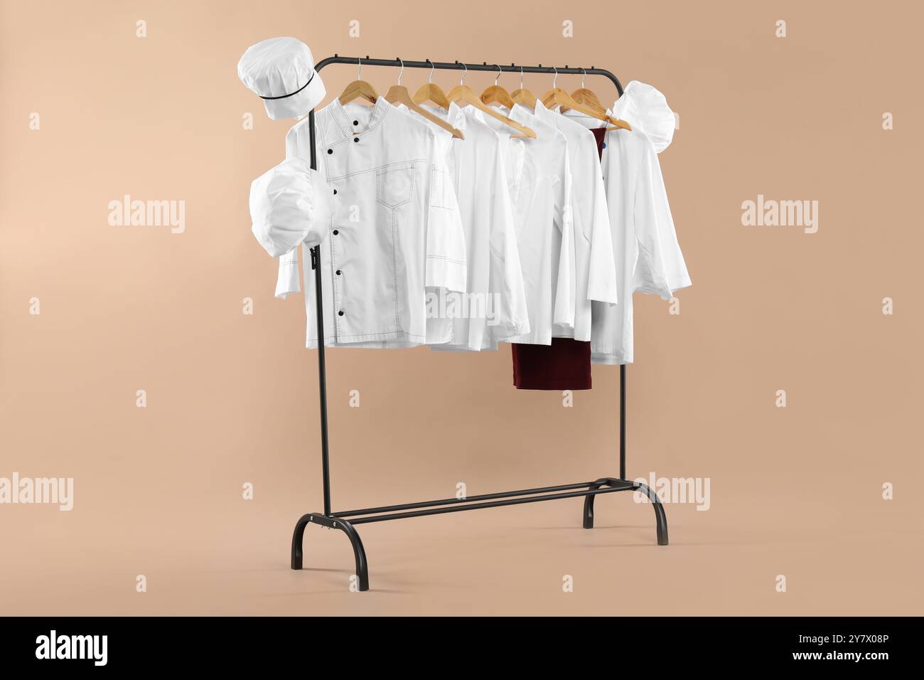 Different chef's uniforms on clothing rack against beige background ...