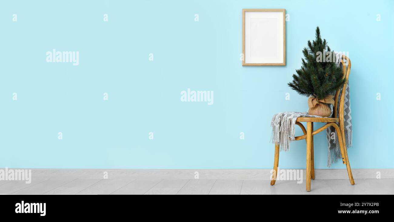 Christmas tree on chair near light blue wall with blank frame. Banner ...