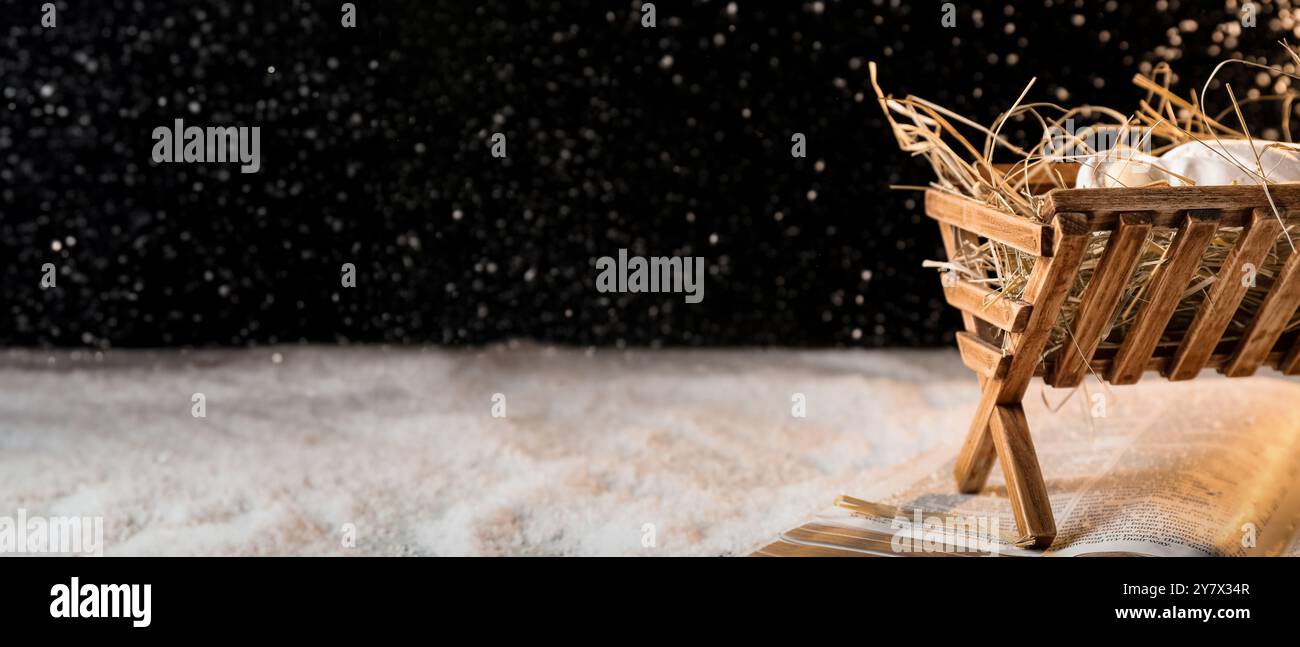 Bible, wooden manger with hay and dummy of baby on snow against black ...