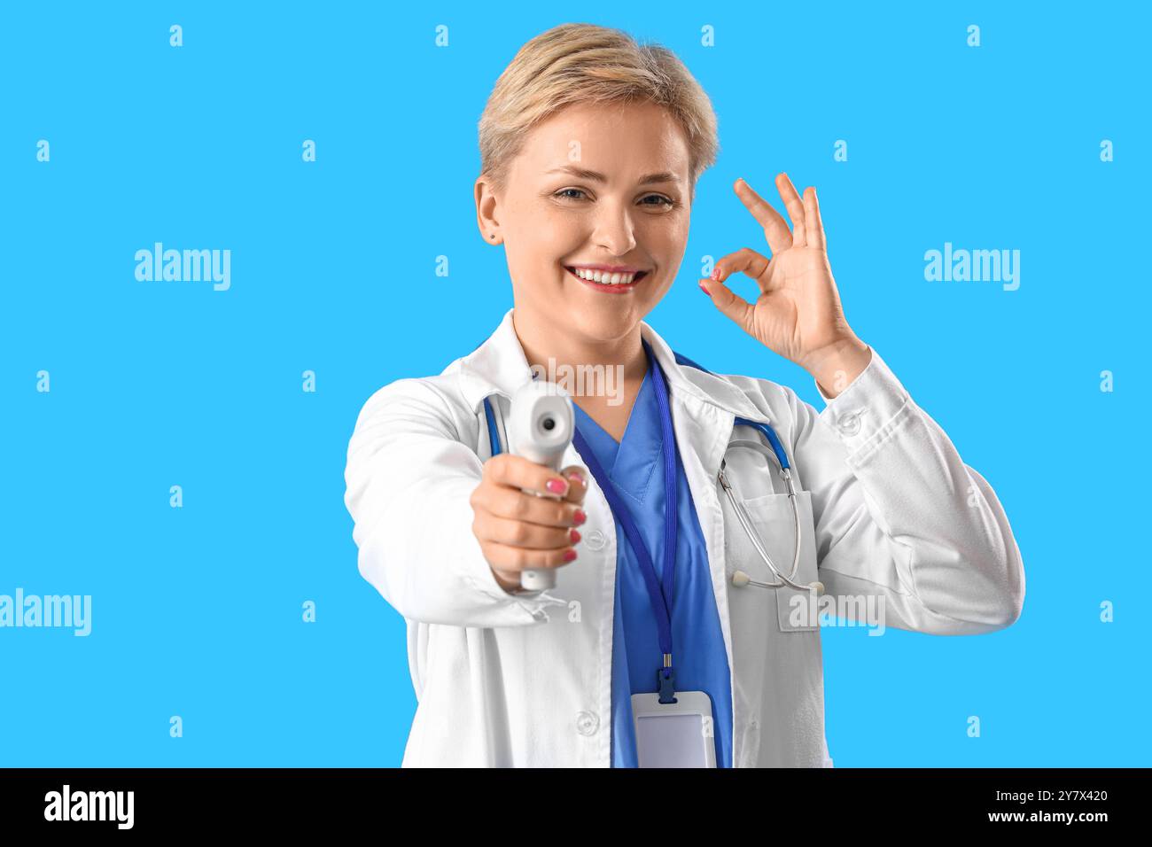 Female medical intern with infrared thermometer on blue background ...