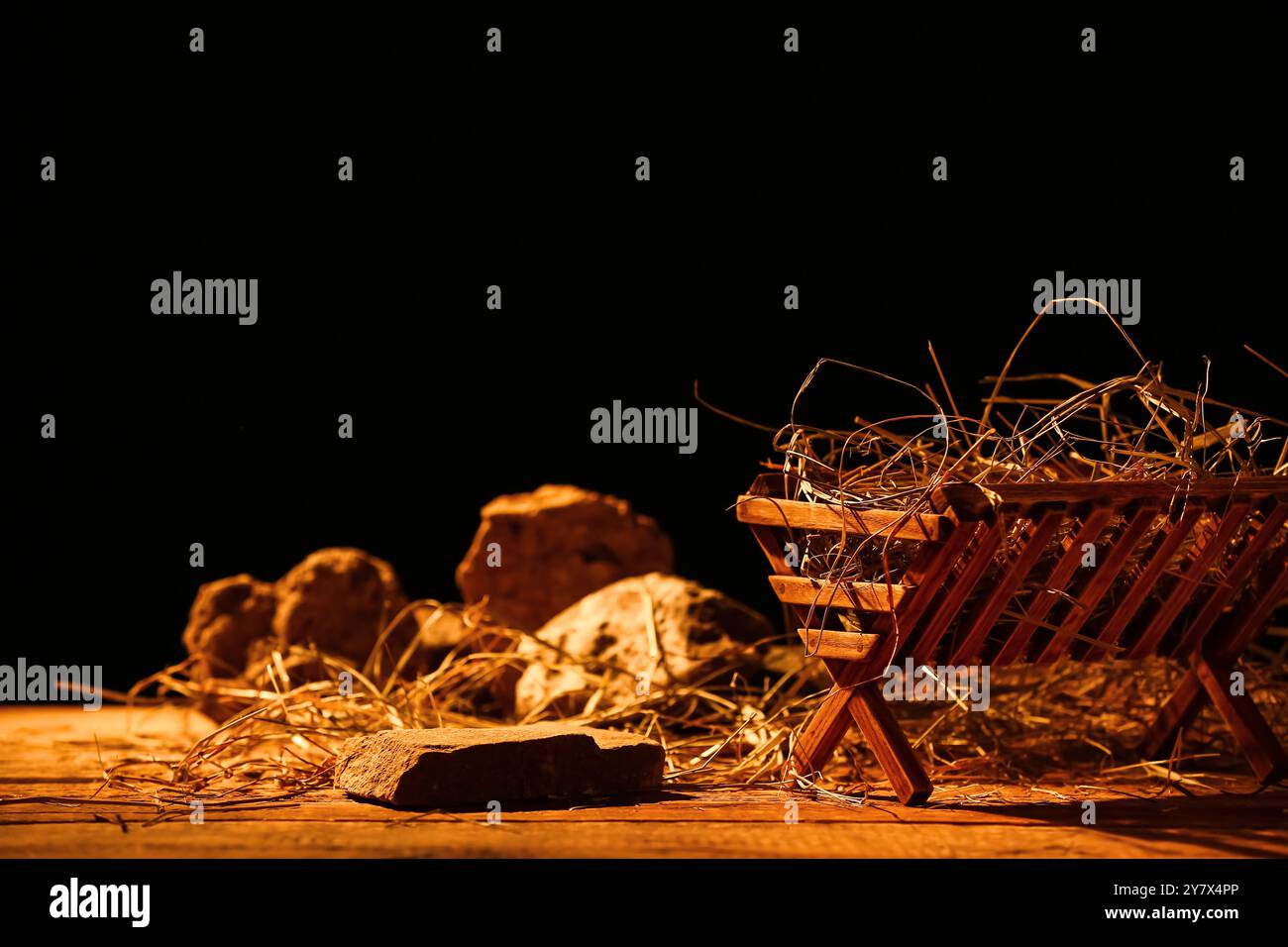 Manger with hay and stones on wooden table against dark background ...