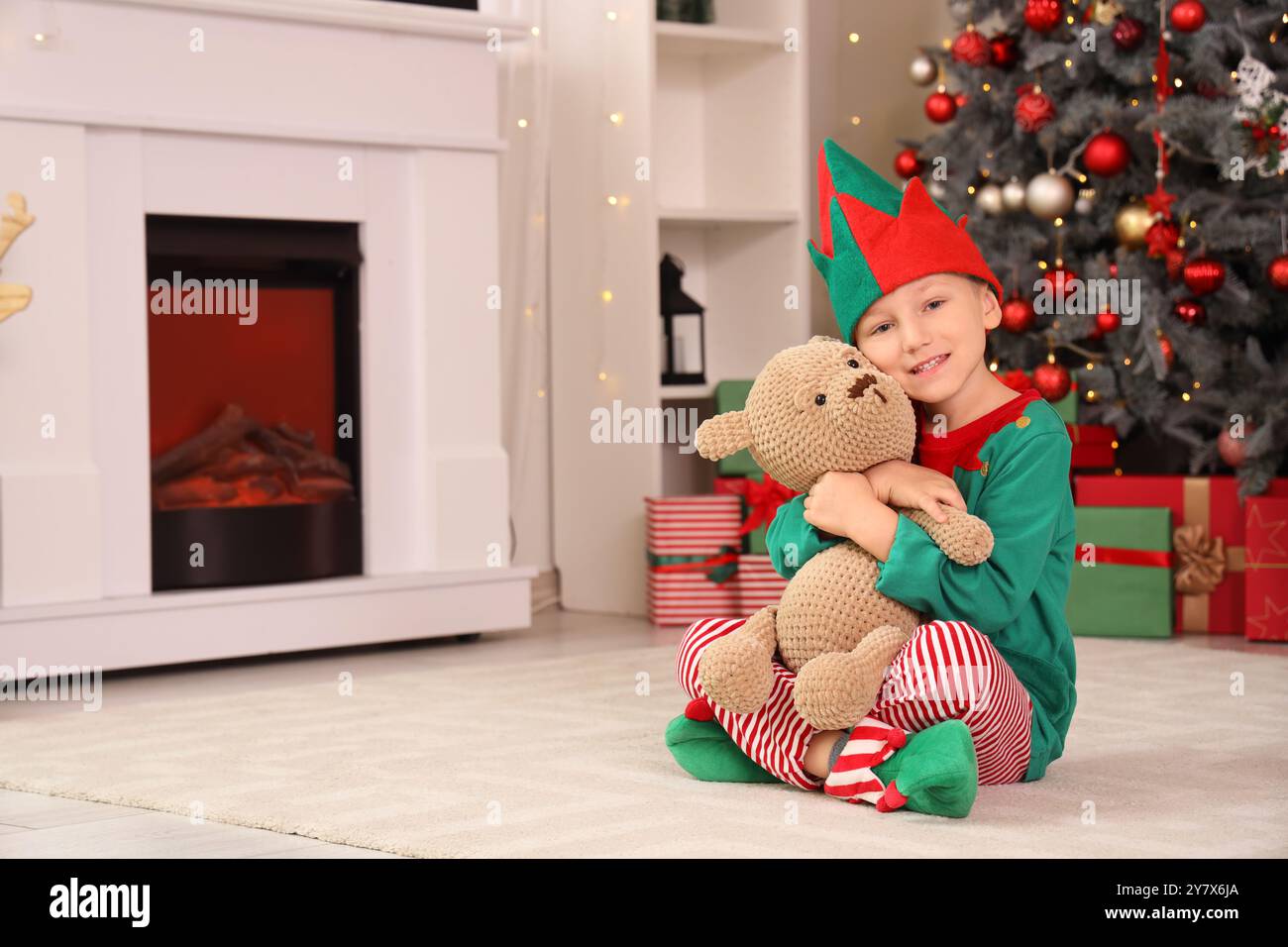 Cute little boy in elf costume with toy bear at home on Christmas eve ...