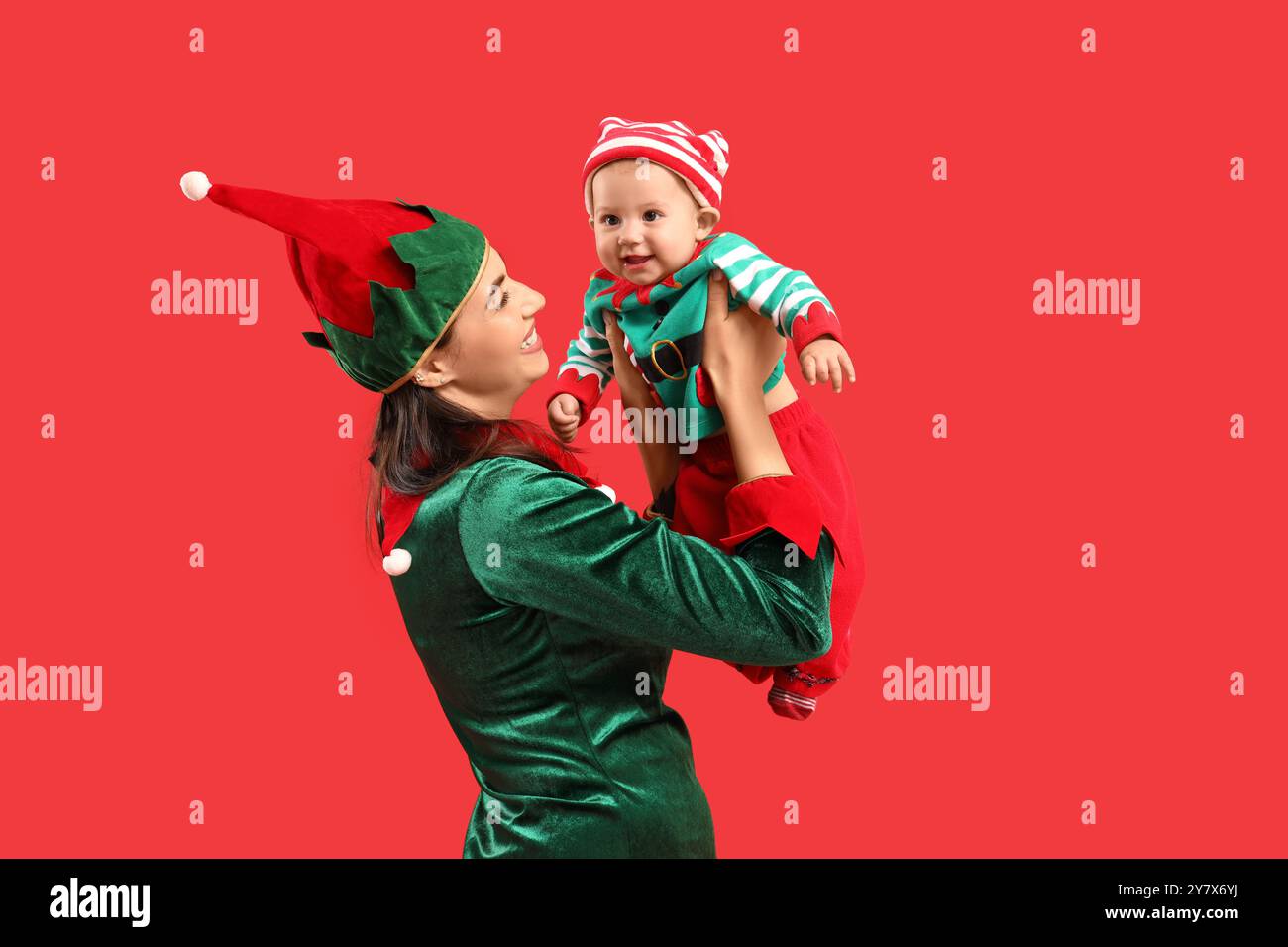 Young mother and cute little baby dressed as elves on red background ...