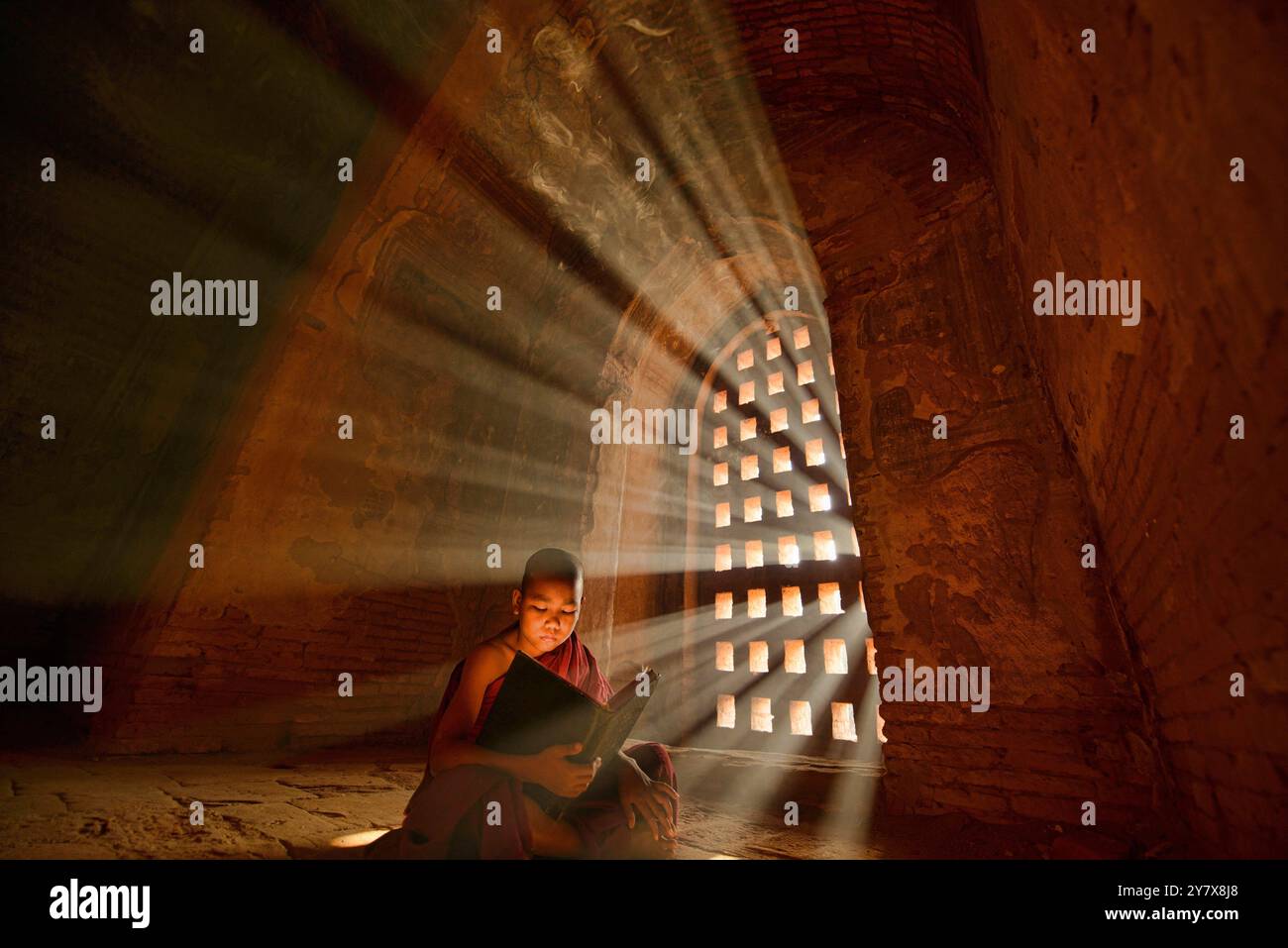 A young monk reading with rays of sunlight in the temples of Bagan ...