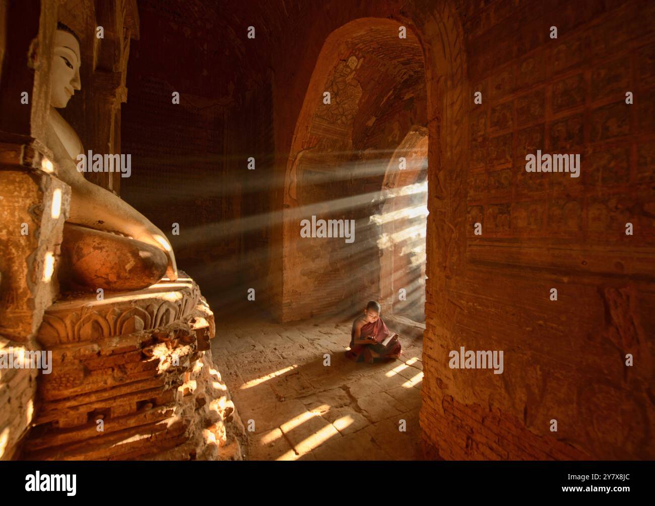 A young monk reading with rays of sunlight in the temples of Bagan ...