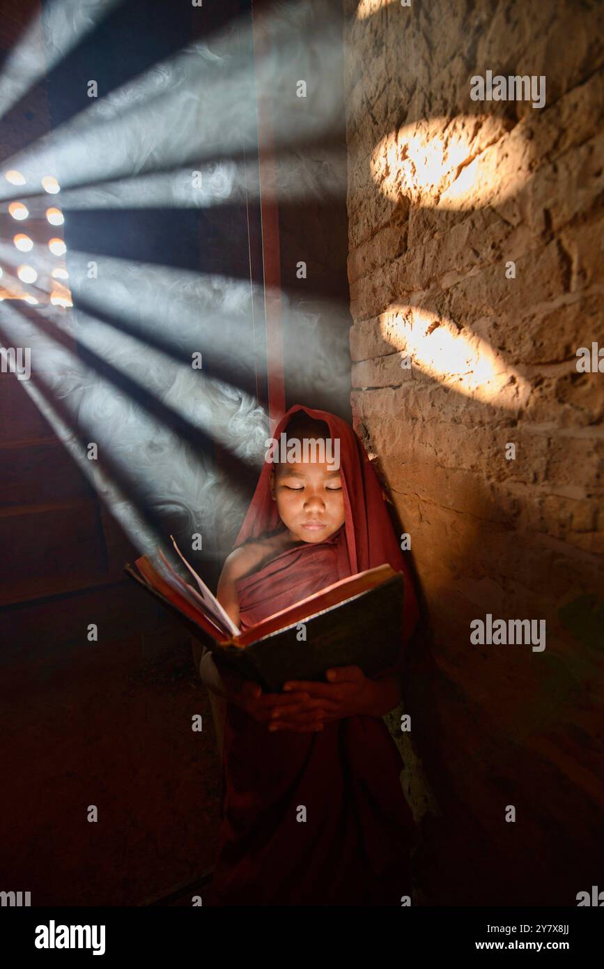 A young monk reading with rays of sunlight in the temples of Bagan ...