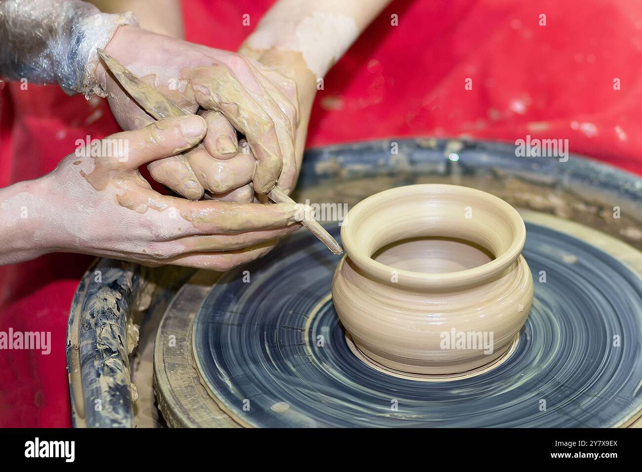 Two pairs of hands mold something from clay on a potter's wheel. Master ...