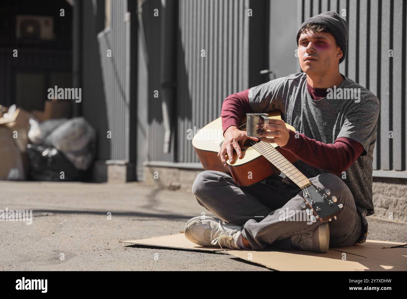 Young homeless man with cup playing guitar on street Stock Photo - Alamy