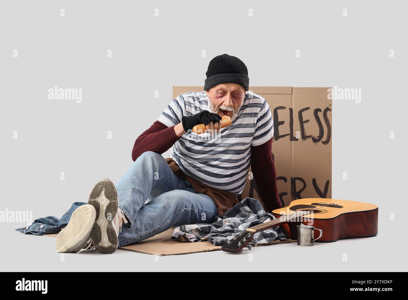 Mature homeless man eating bread on light background Stock Photo - Alamy