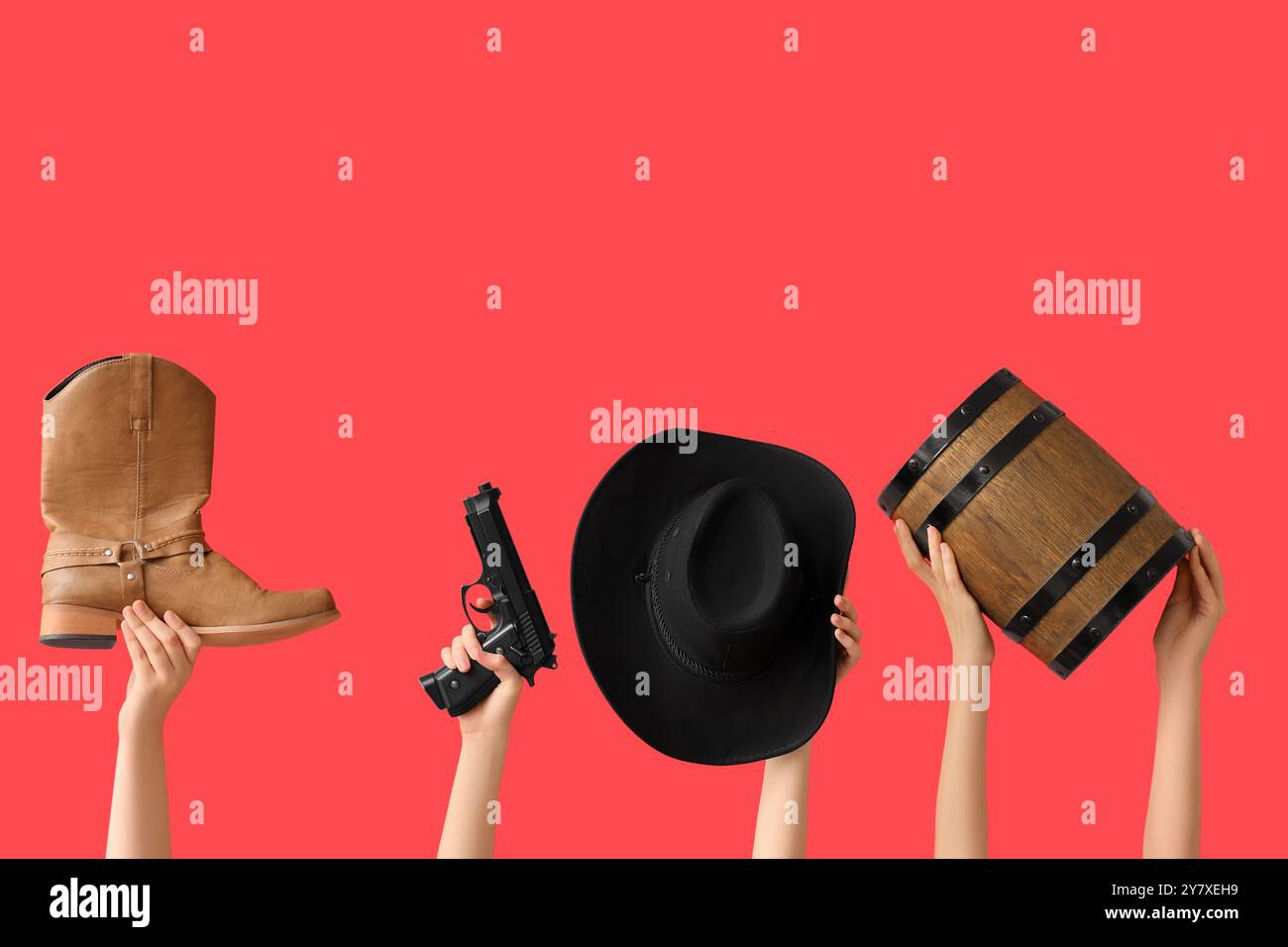 Female hands with gun, cowboy hat, shoe and barrel on red background ...