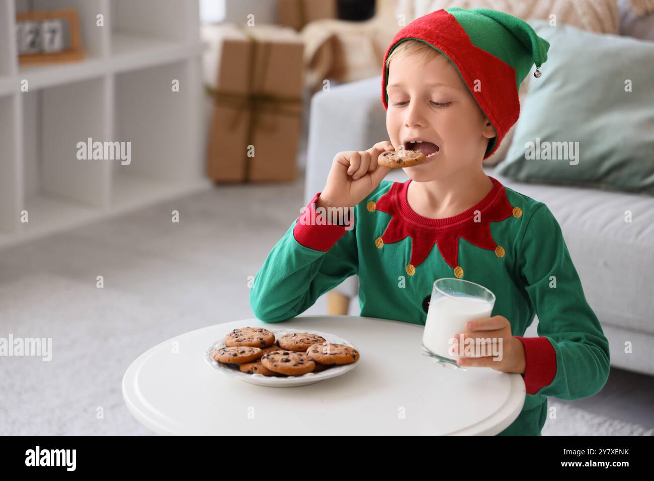 Cute little boy dressed as Christmas elf eating cookies with cup of ...