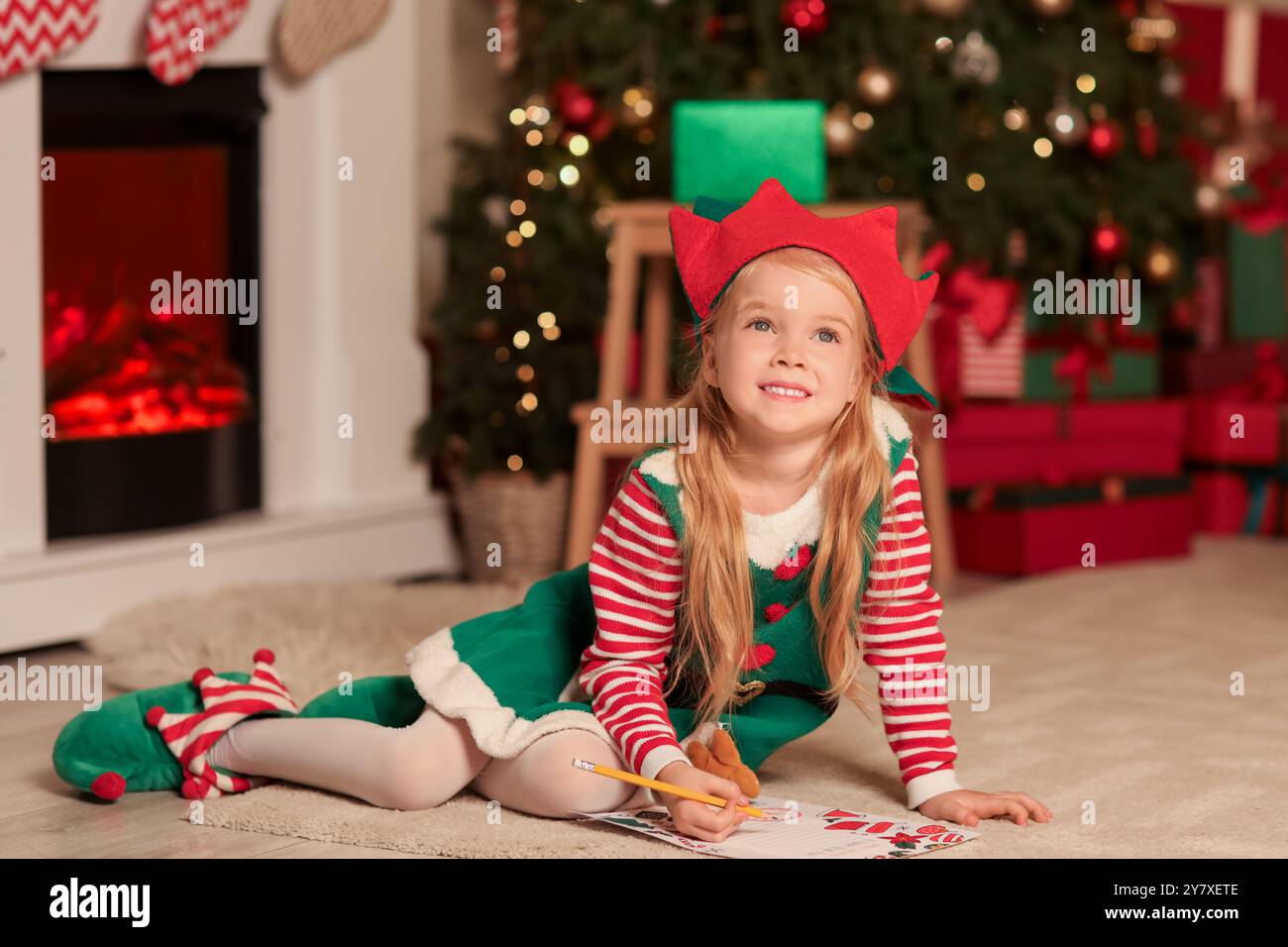 Cute little girl in elf costume writing letter to Santa at home on ...