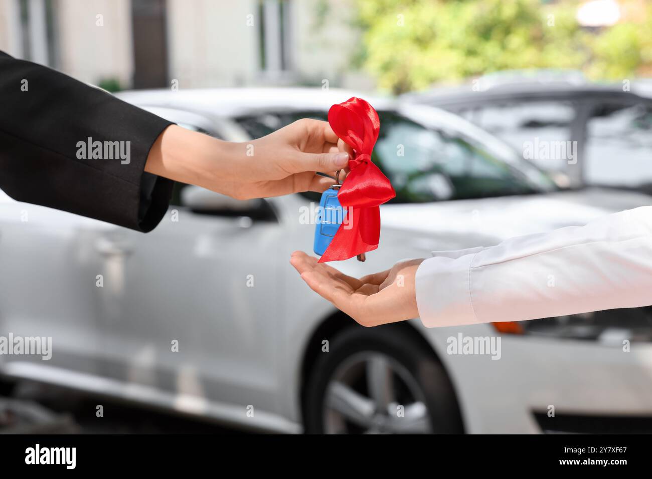 Woman giving gift keys of automobile to new owner in car showroom ...