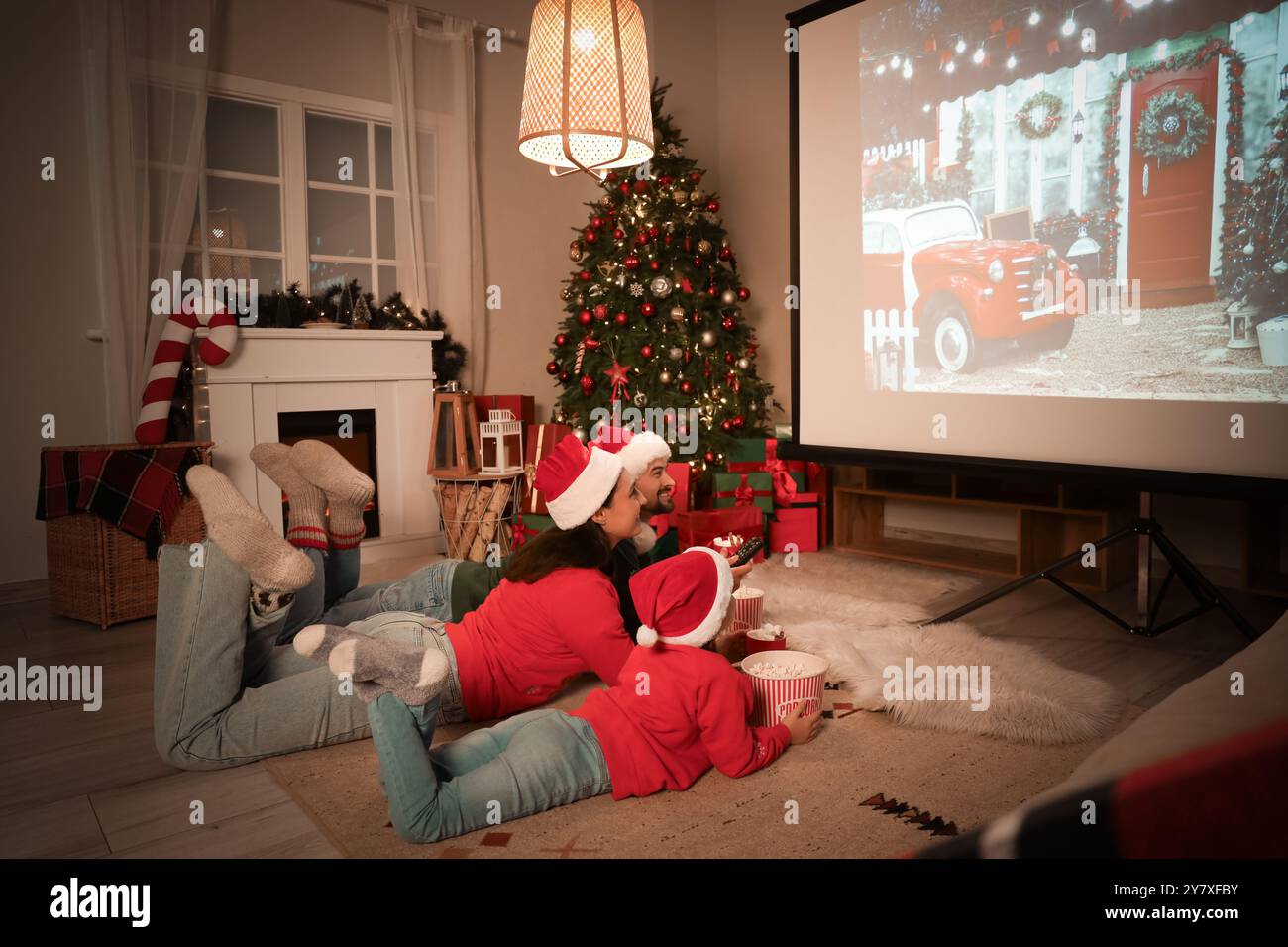 Little girl with her parents in Santa hats and popcorn watching ...