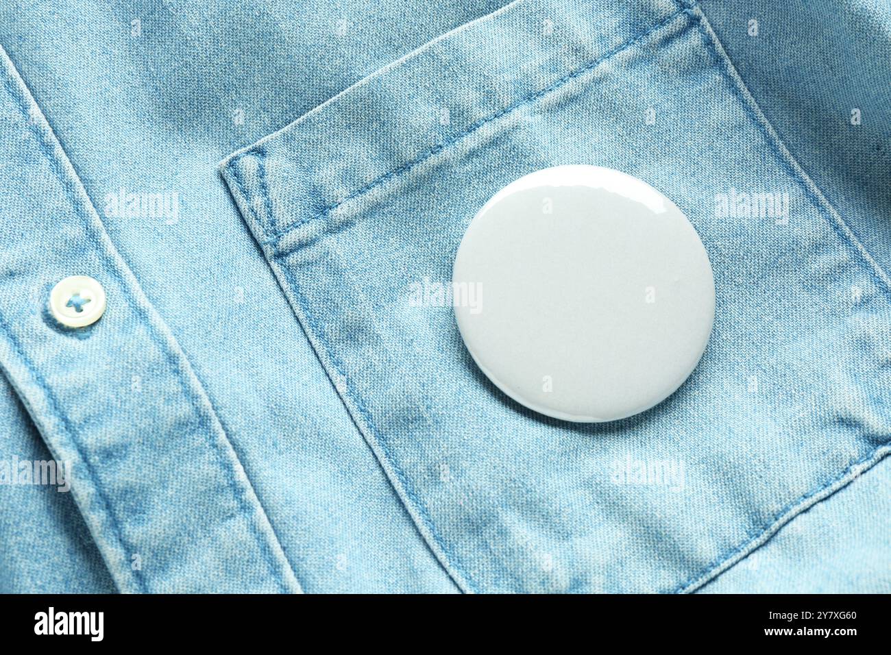 White button badge pinned on denim shirt, top view. Mockup for design ...