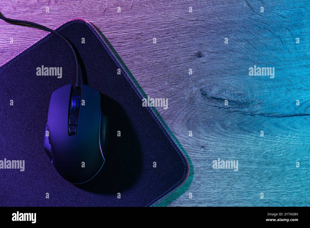 Black computer mouse and mousepad on wooden table in neon lights, top ...