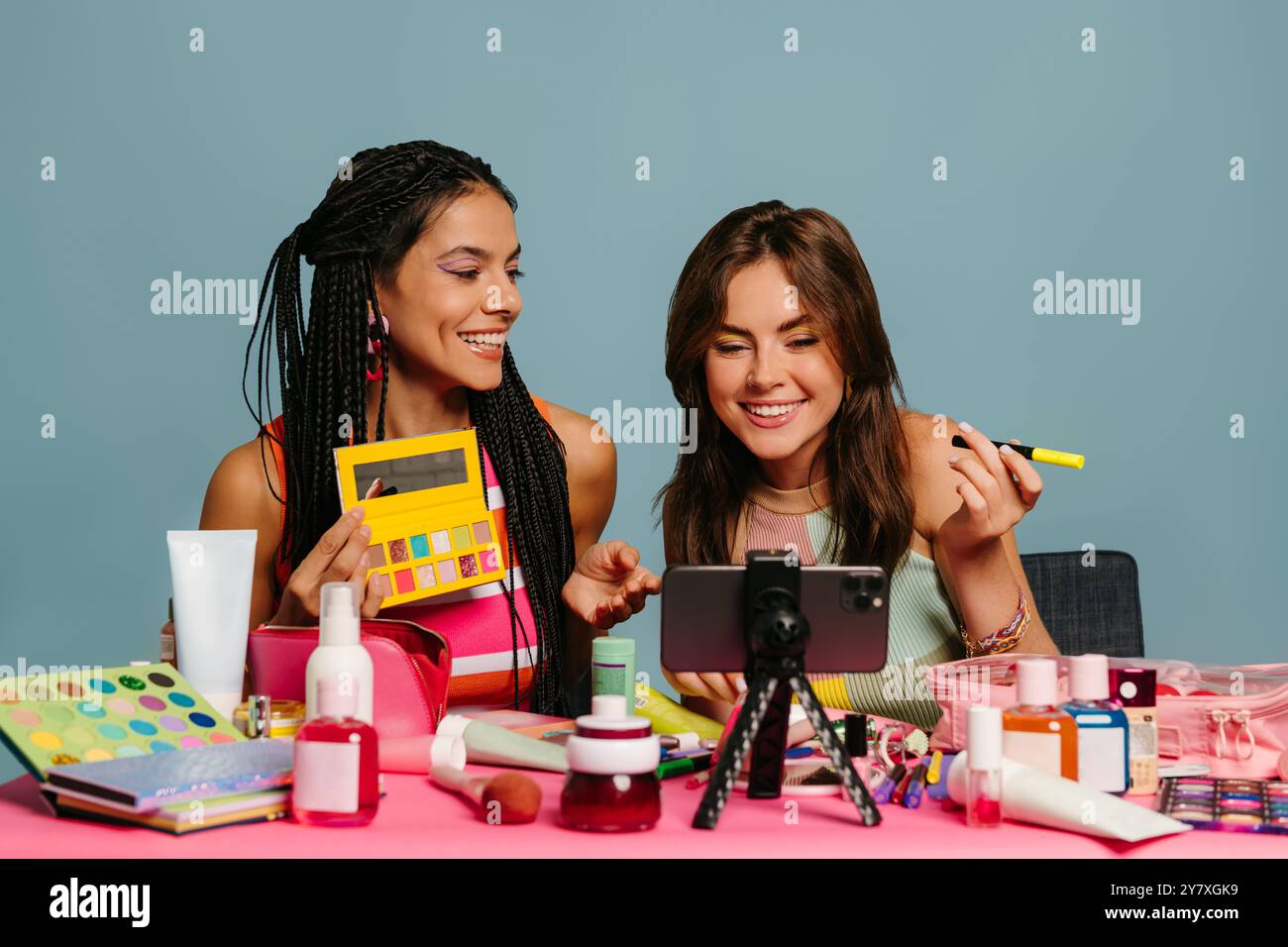 Two cheerful female presenters streaming beauty vlog while sitting at ...