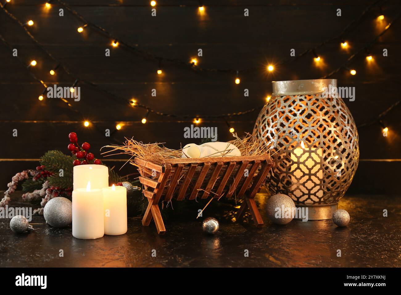 Manger with baby, fir branches, burning candles and glowing lights on ...