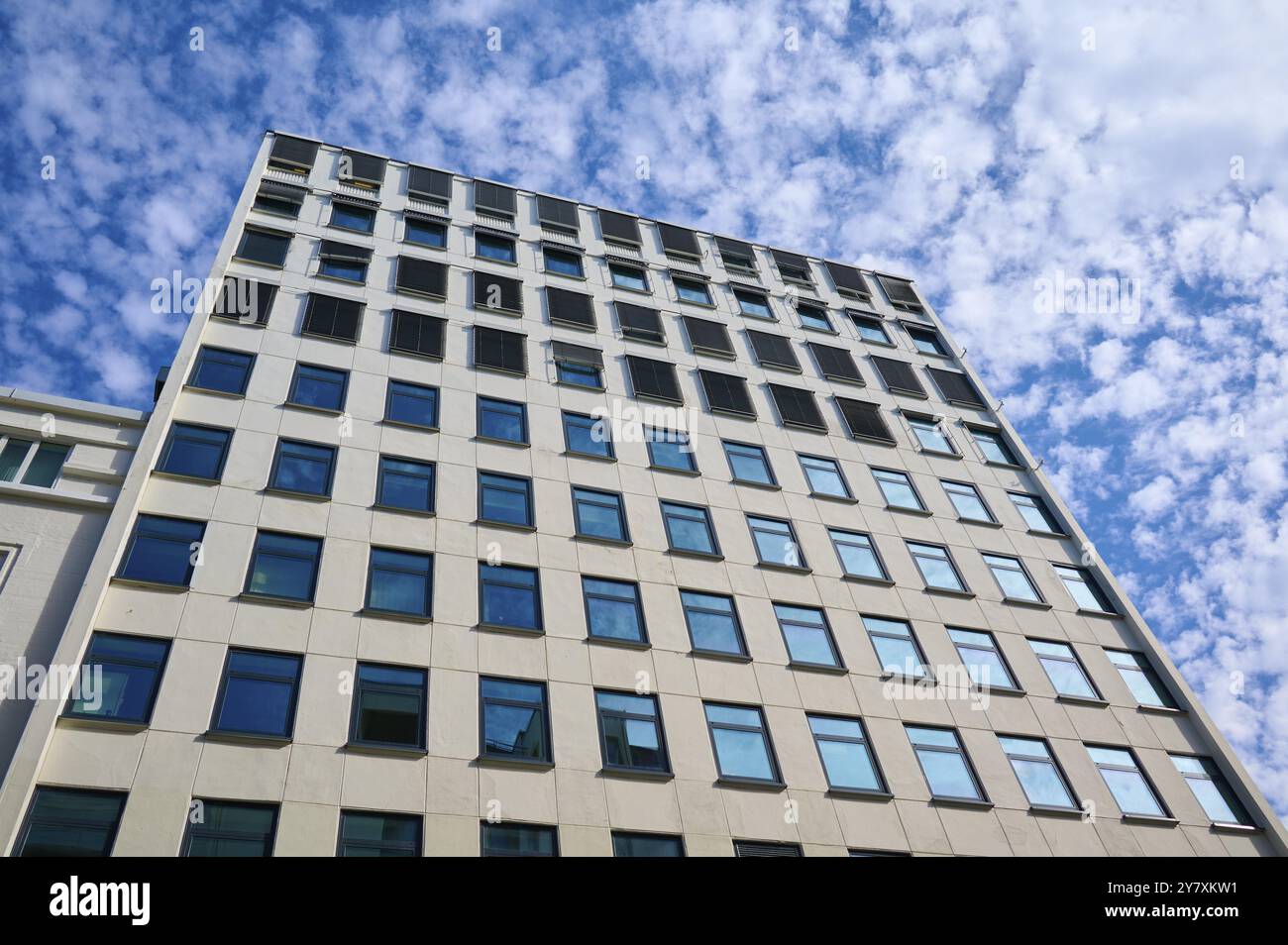 A modern skyscraper with many glass windows stands in front of a cloudy ...